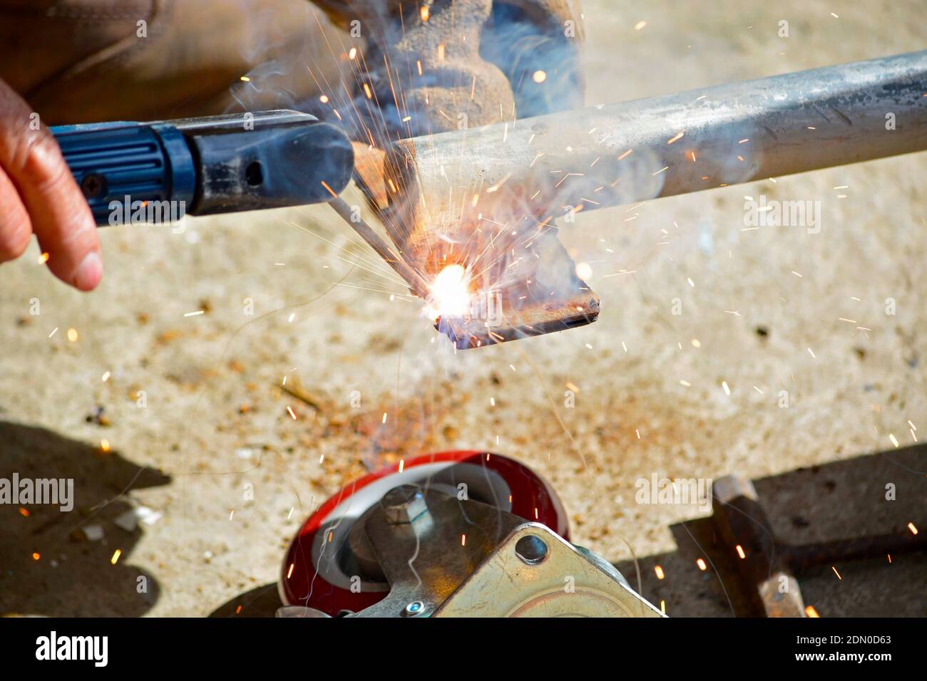 Worker with a welding machine fixing a caster wheels with fiery sparks ...