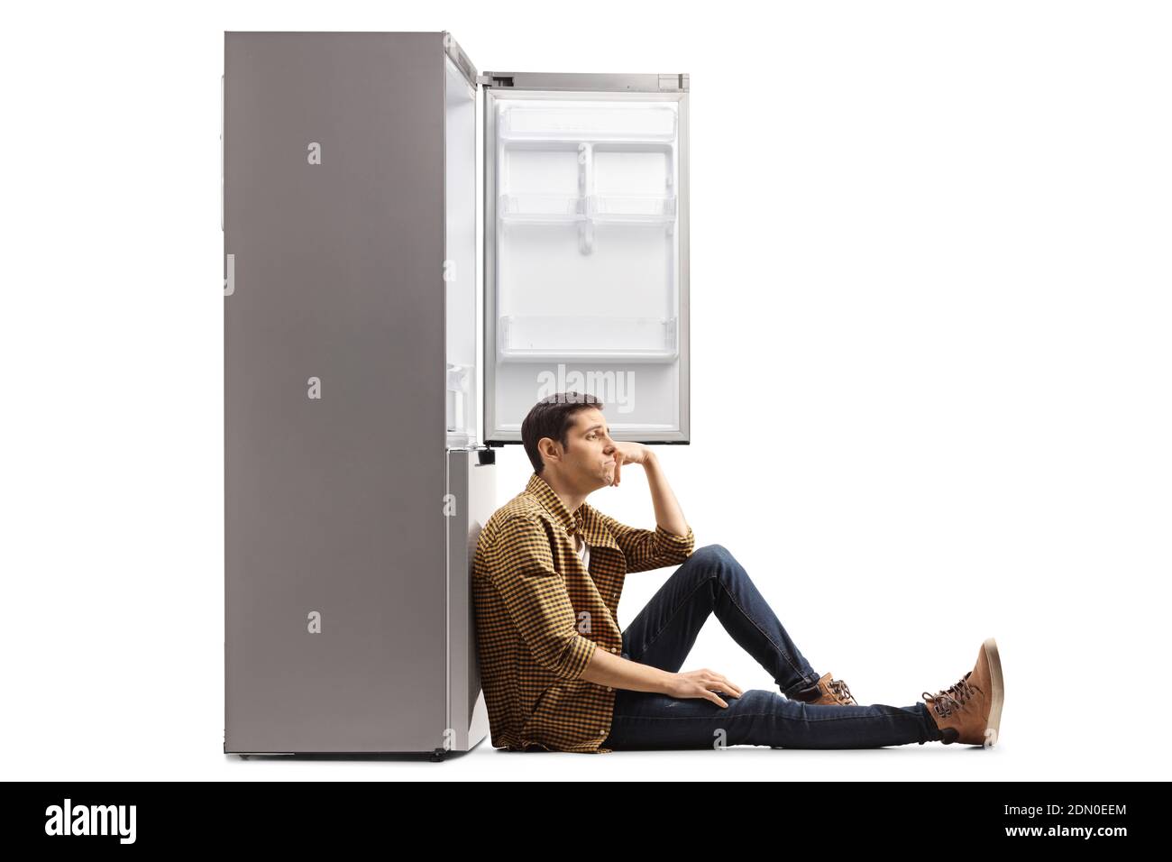 Sad young man sitting in on the floor and leaning on an empty fridge ...