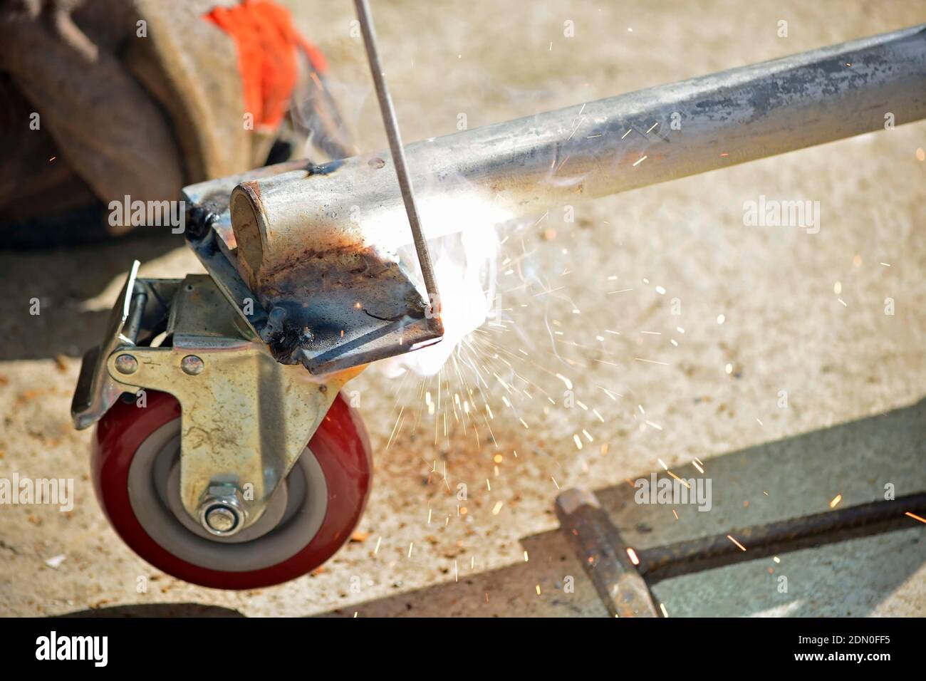 Worker with a welding machine fixing a caster wheels with fiery sparks ...
