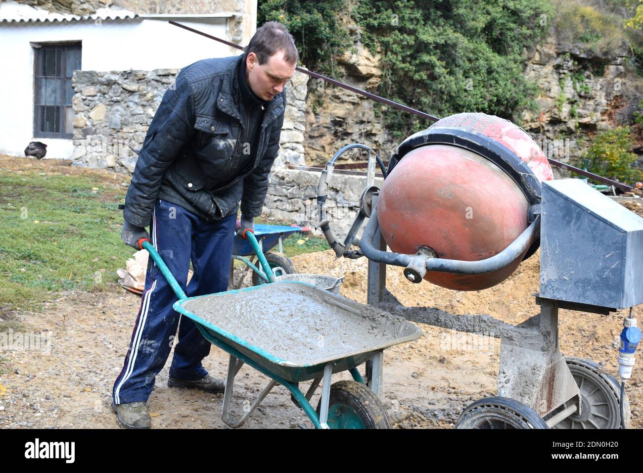 Bricklayer next to concrete mixer carrying a concrete wheelbarrow Stock ...