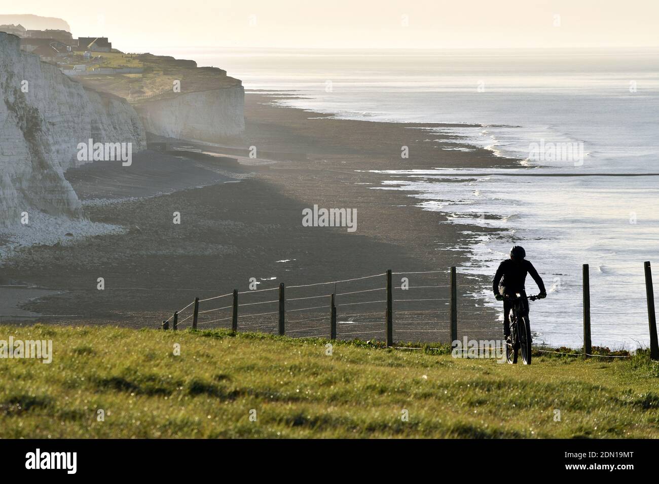 Silhouette of cyclist riding along scenic coastal pathway near dramatic ...