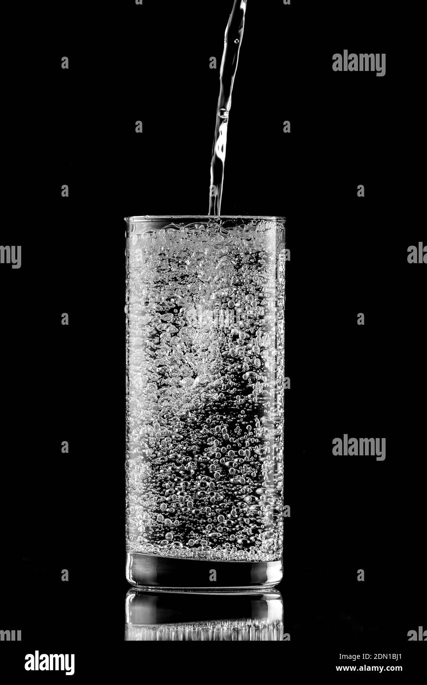 Pouring water into a glass on a black background Stock Photo - Alamy