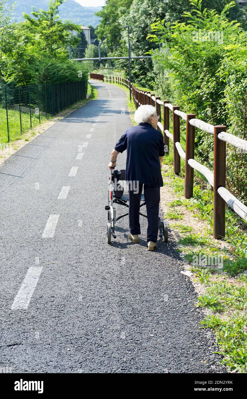 Handicapped senior lady with a walking disability pushing her walker on ...