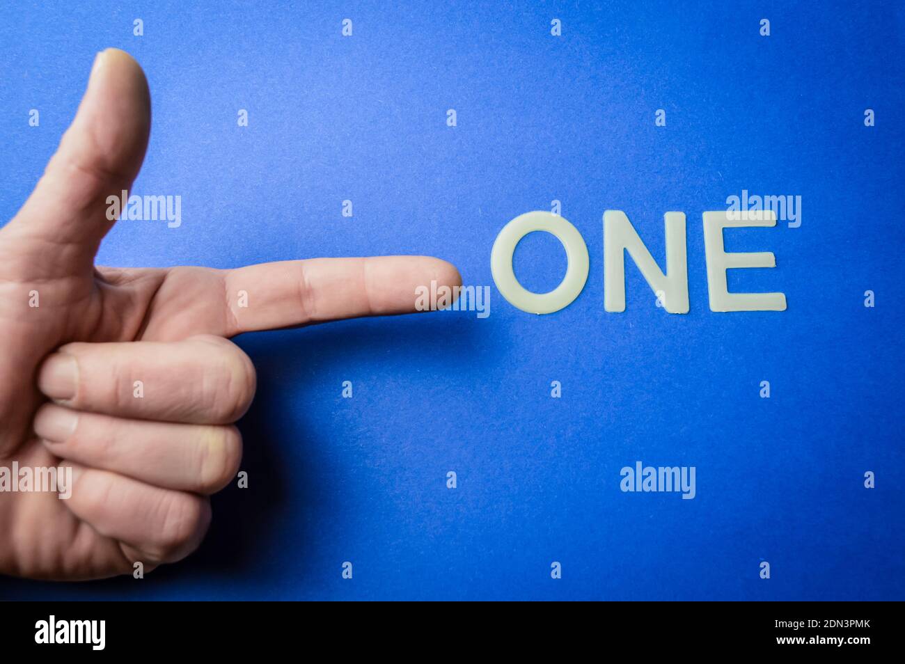 Human hand pointing the word One written with plastic letters on blue ...