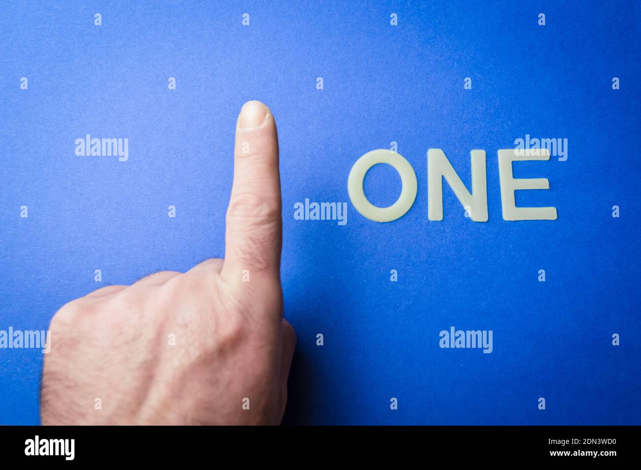 Human finger beside the word One written with plastic letters on blue ...