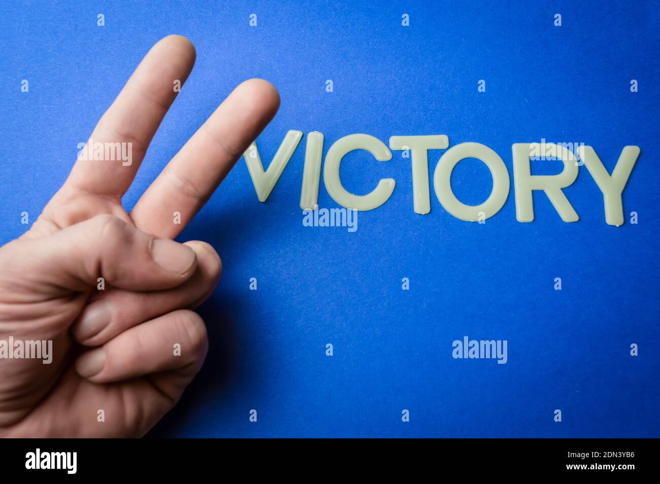 Human hand making a victory sign beside the word written with plastic ...