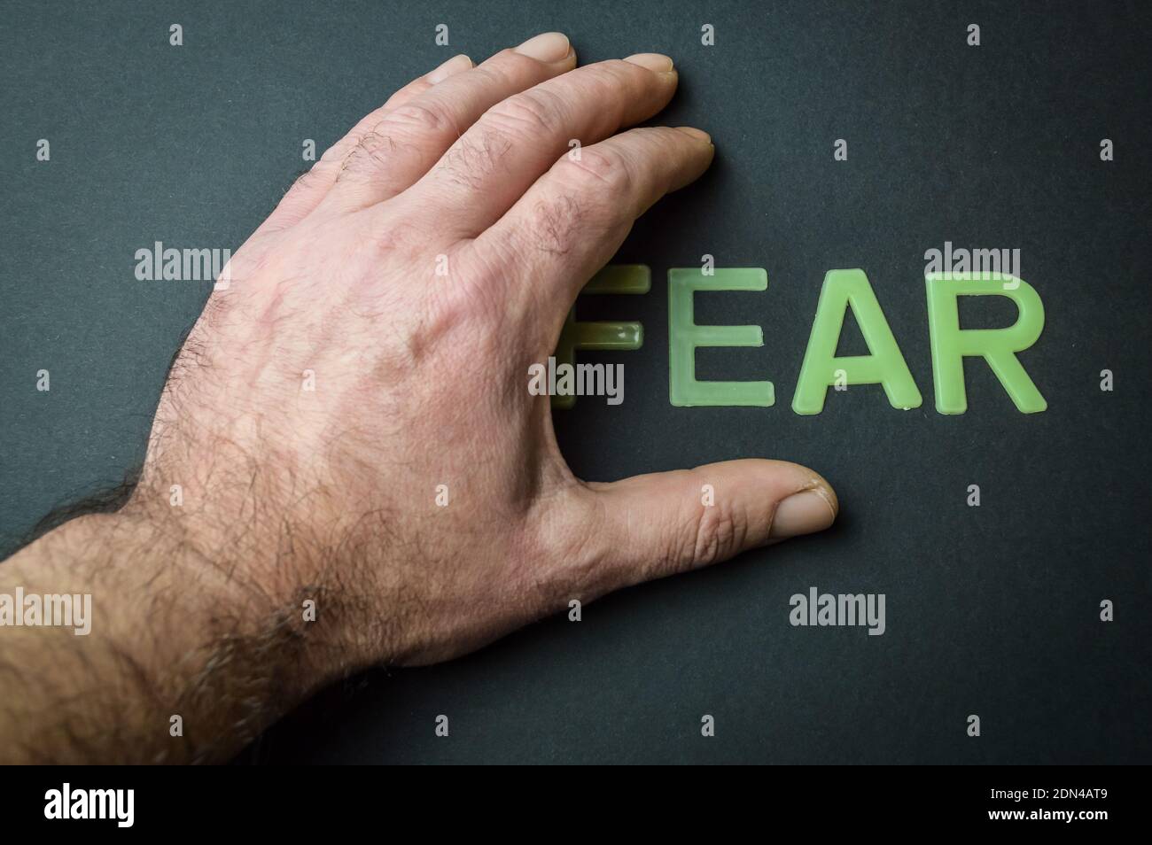 Human hand hides the word Fear written with plastic letters on dark ...