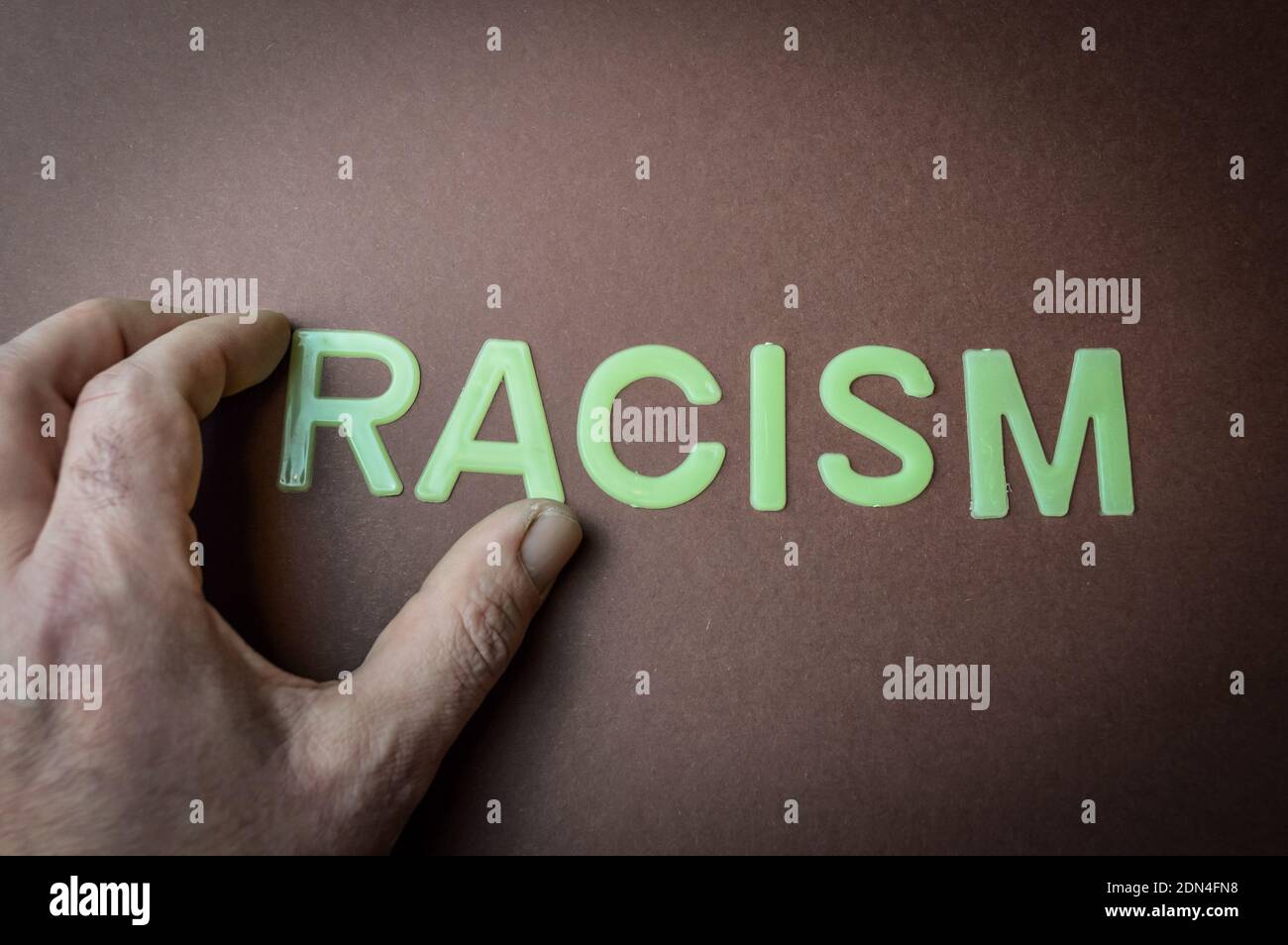 Human fingers holding the word Racism written with plastic letters on a ...