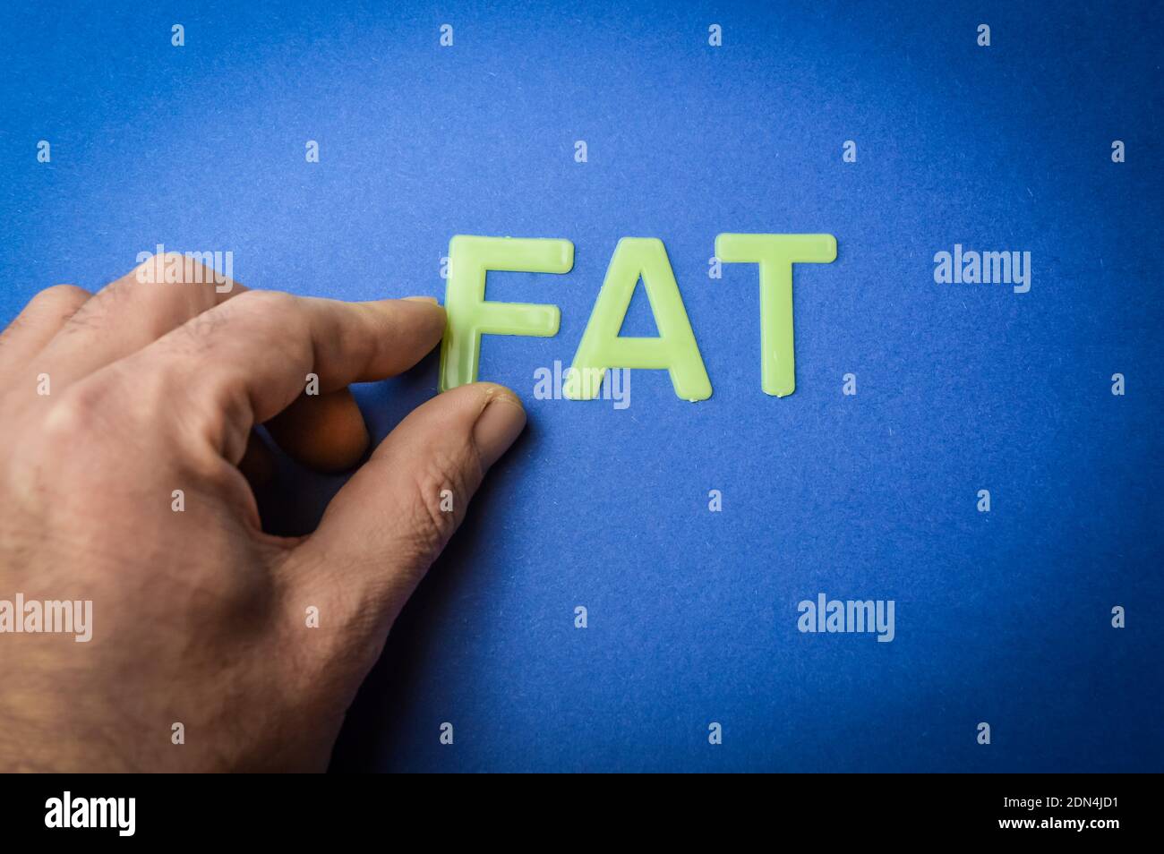 Human fingers removes the word Fat written with plastic letters on blue ...