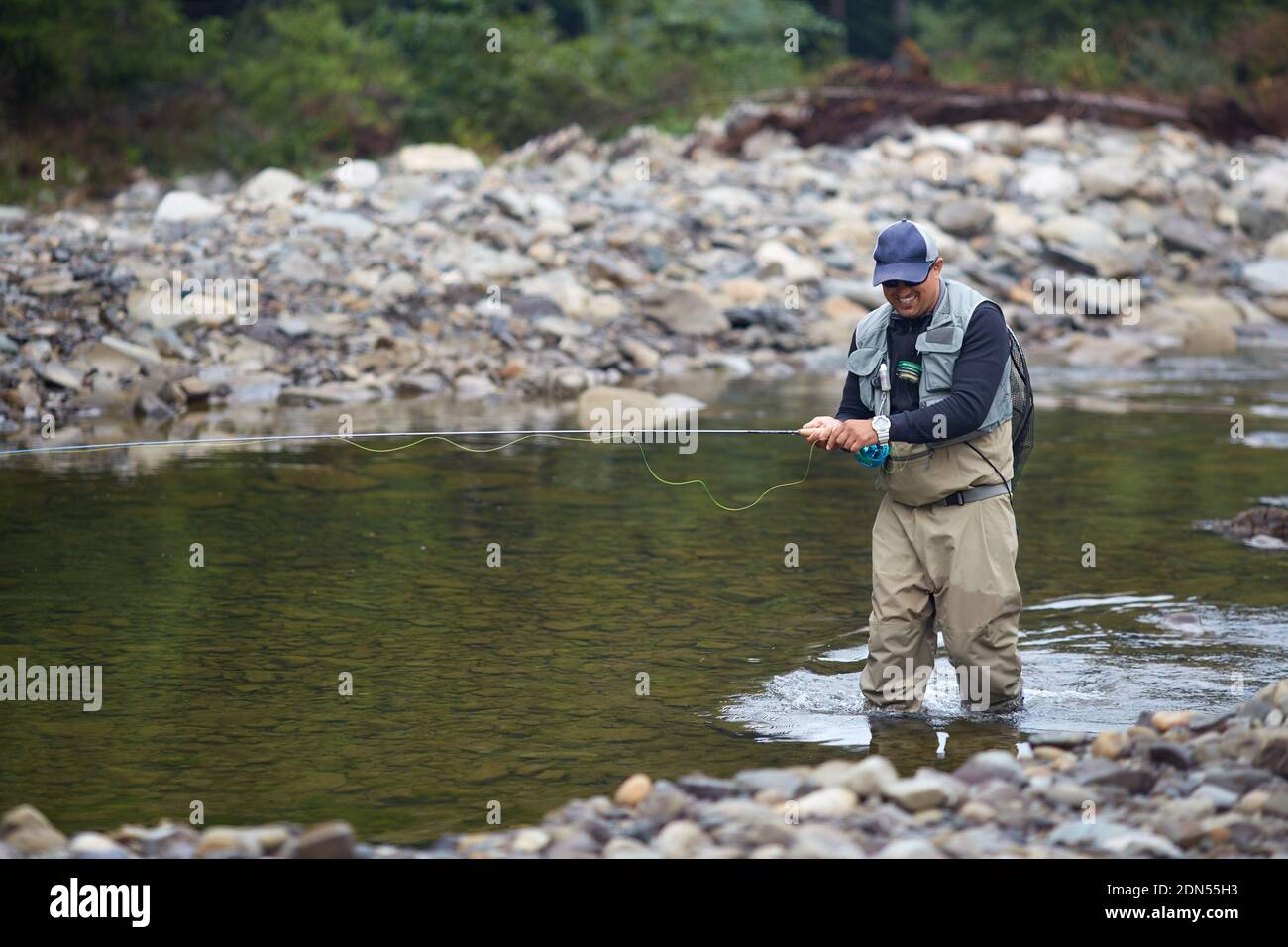 Smiling man walking in river in waterproof clothing and fishing with ...