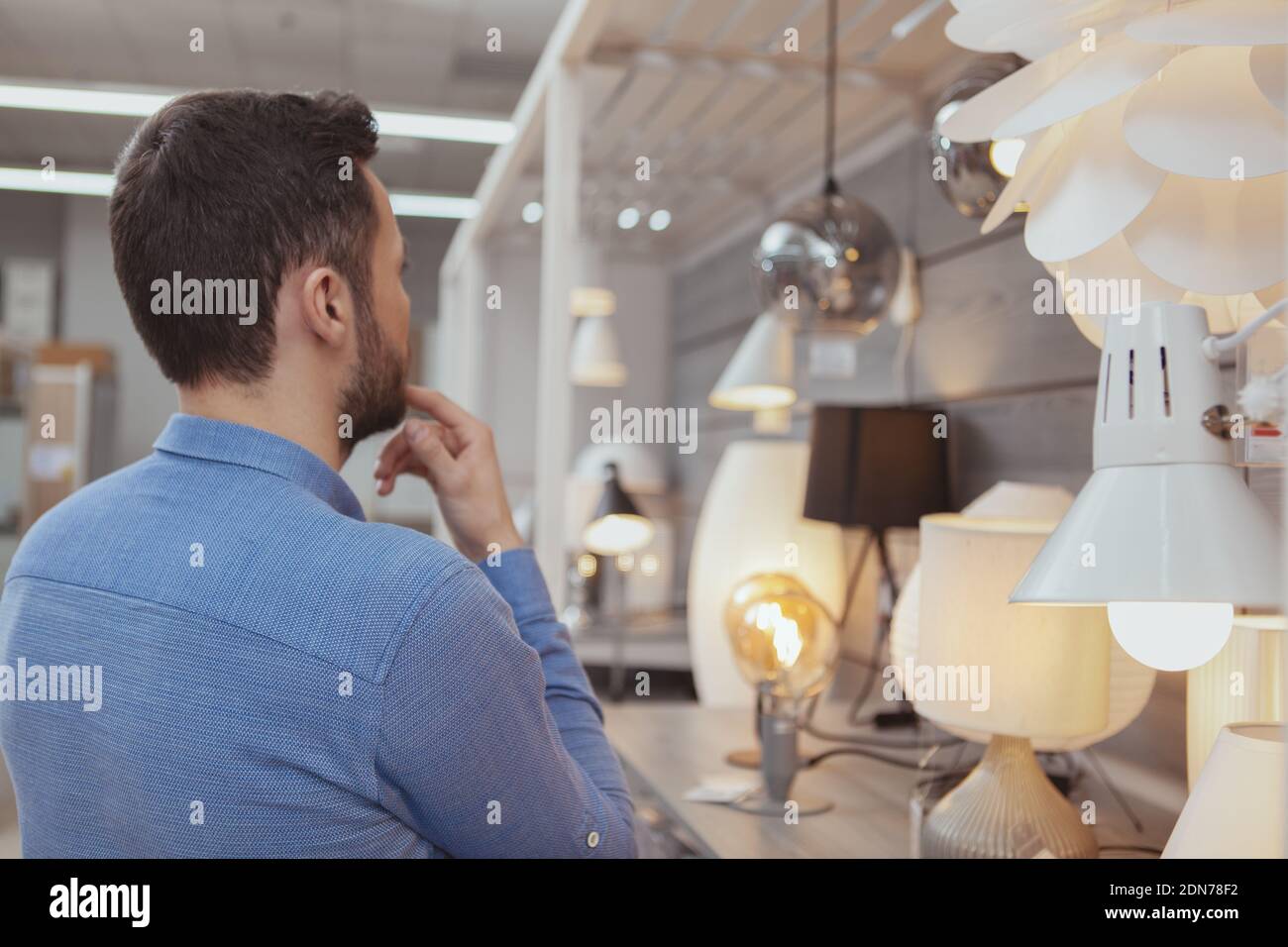 Rear view shot of a male customer choosing lighting for his apartment ...