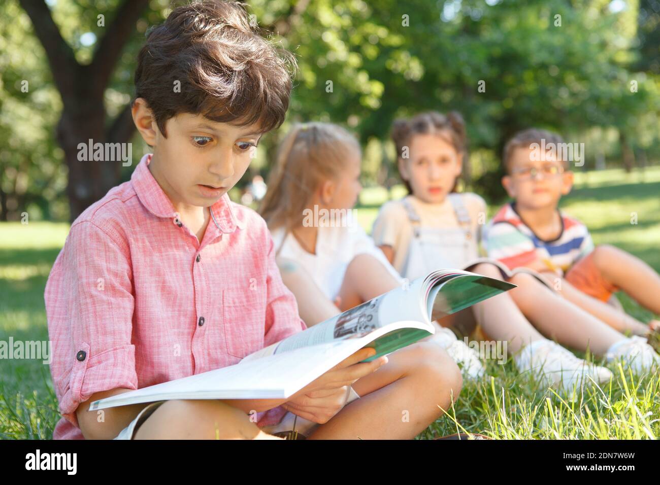 Cute little boy looking overwhelmed, reading a book at public park ...