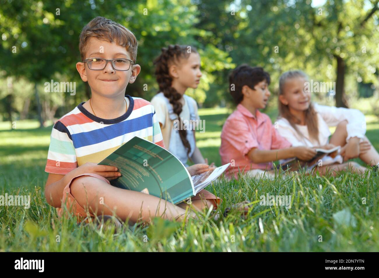 Charming little boy smiling to the camera, while reading a book ...