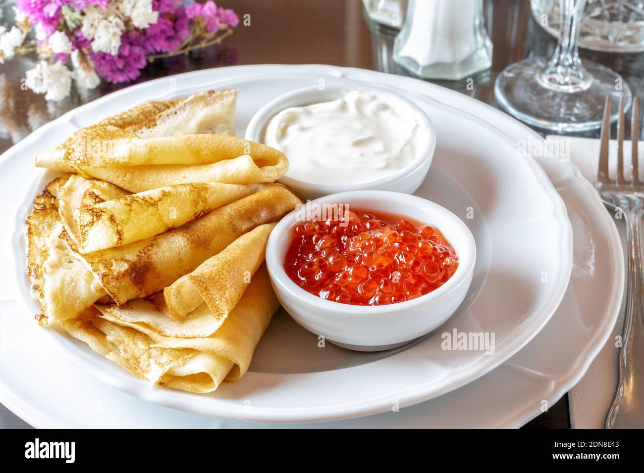 Baked hot crepes with red caviar and sour cream on the white ceramic ...