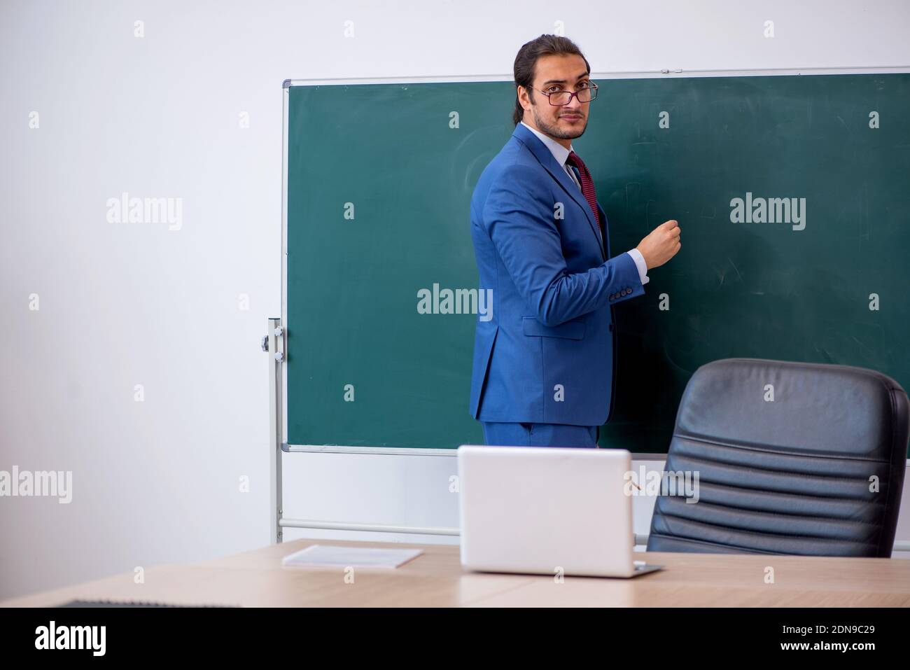 Young teacher in suit in front of green board Stock Photo - Alamy