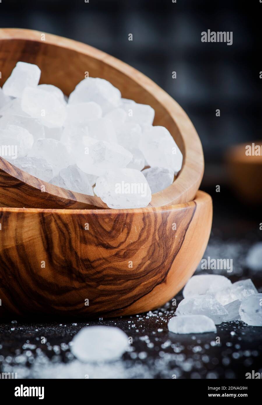 White crystal candy sugar in wooden bowl on black table, selective ...