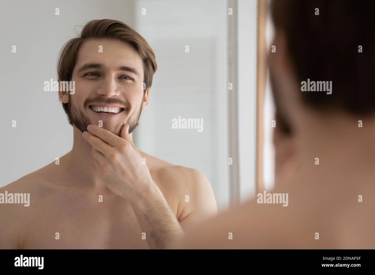 Smiling young 30s handsome well-groomed man looking in mirror Stock ...