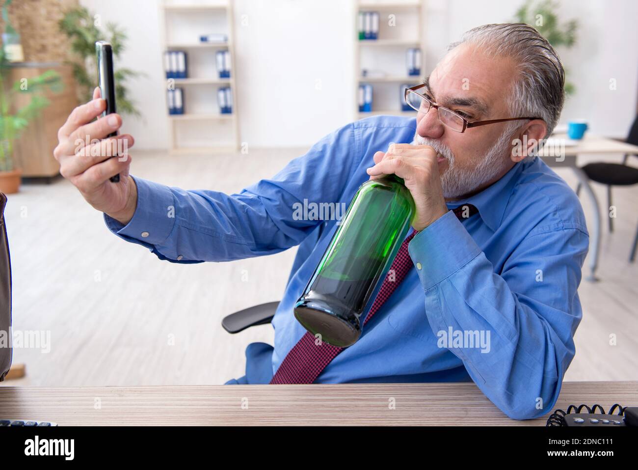 Senior male employee drinking alcohol in the office Stock Photo - Alamy