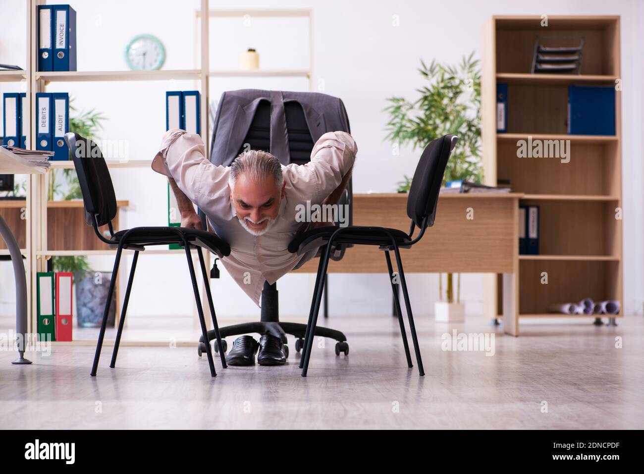 Senior male employee doing physical exercises at workplace Stock Photo ...