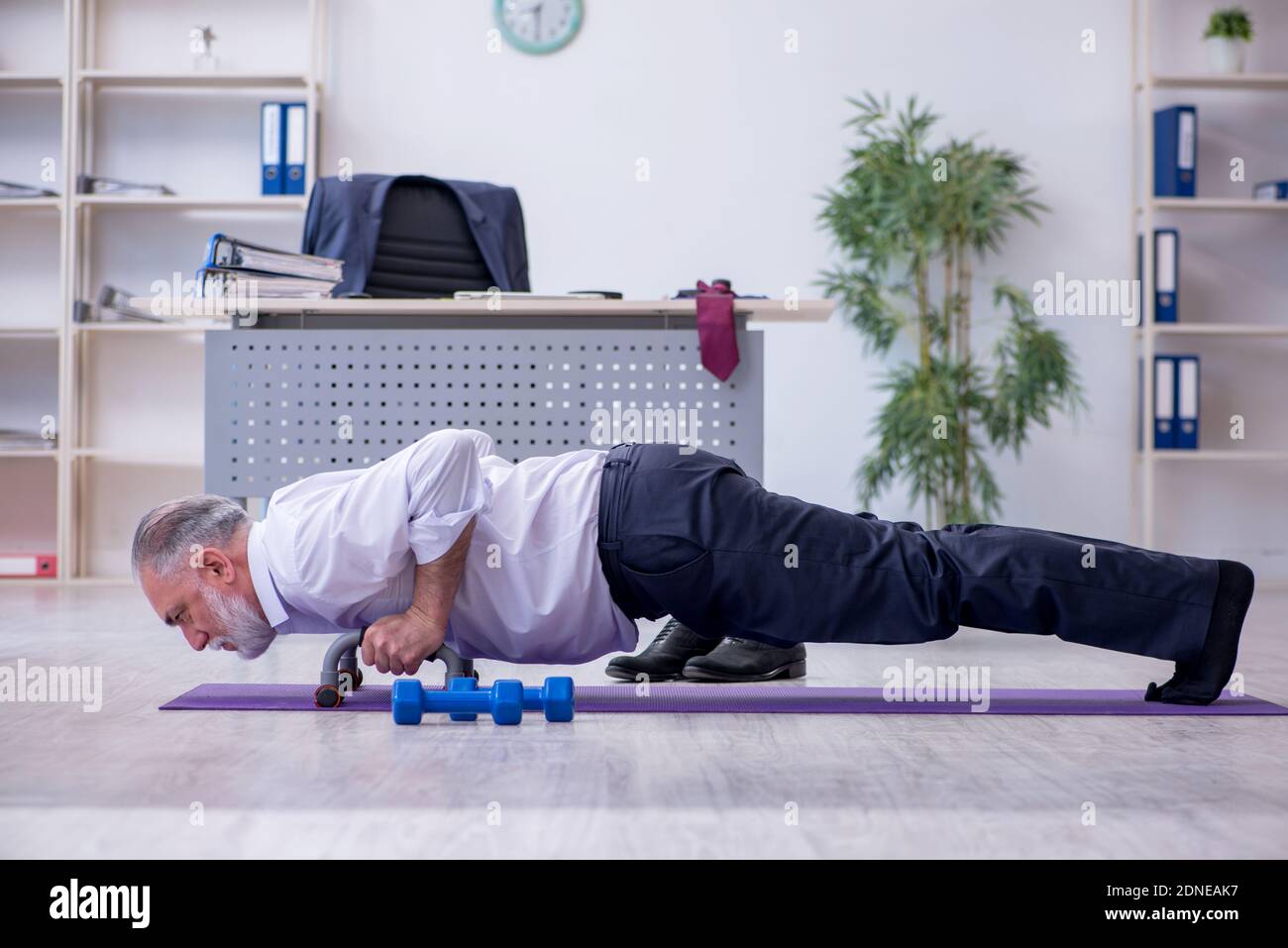 Aged employee doing physical exercises during break Stock Photo - Alamy