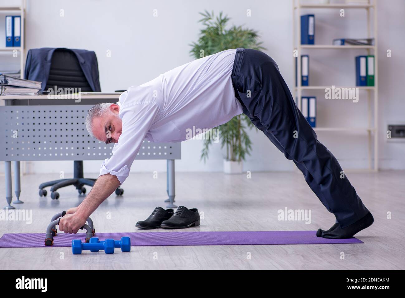 Aged employee doing physical exercises during break Stock Photo - Alamy