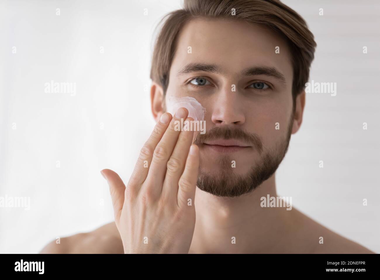 Happy young man applying moisturizing cream on cheek Stock Photo - Alamy