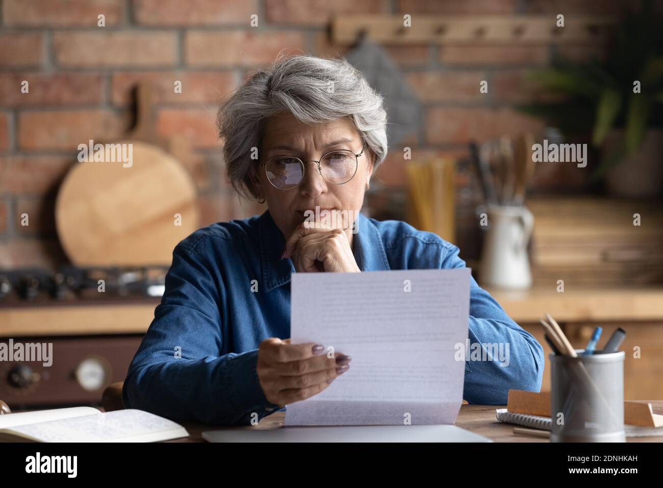 Thoughtful middle aged woman in eyeglasses reading paper letter ...