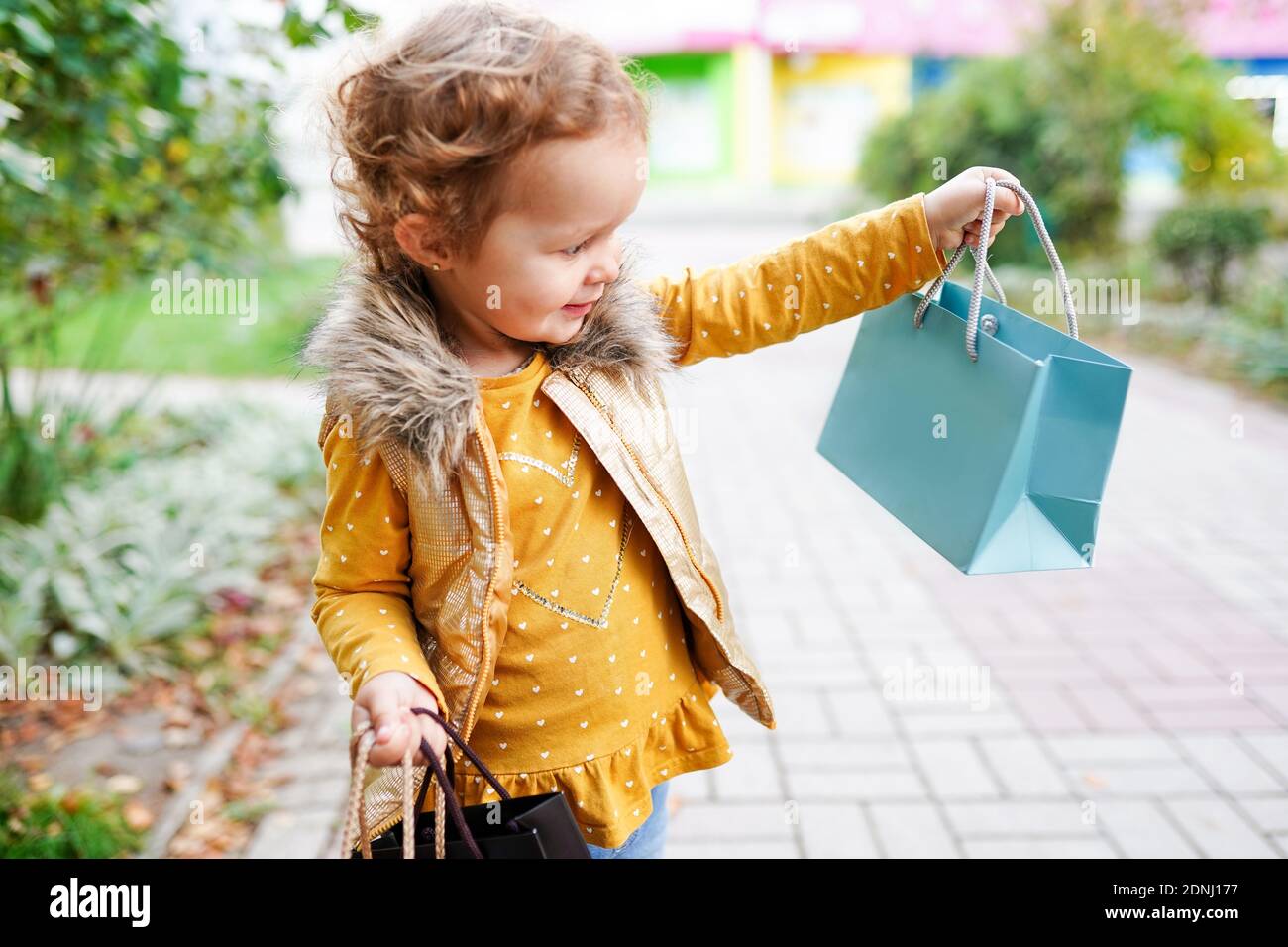 Pretty smiling little girl with shopping bags posing in the park near ...