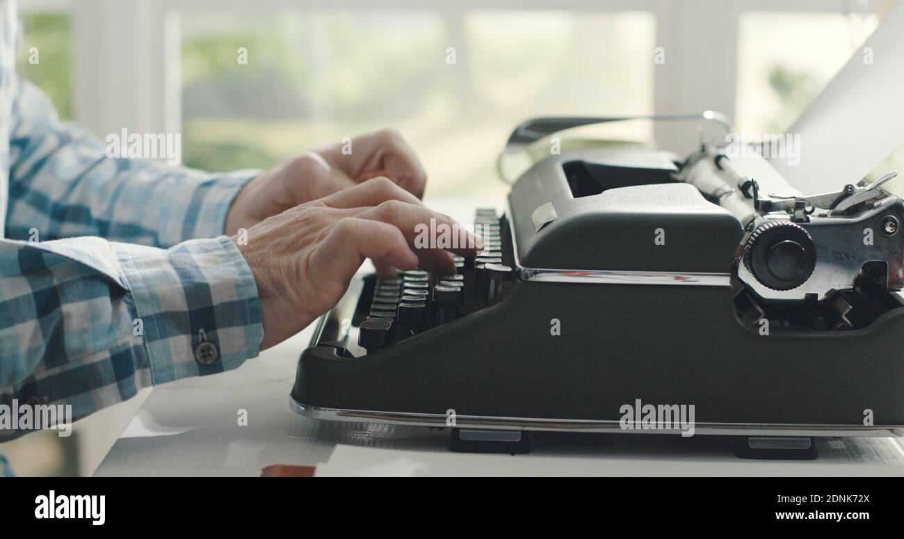 Man sitting at desk at home and typing on a vintage typewriter ...