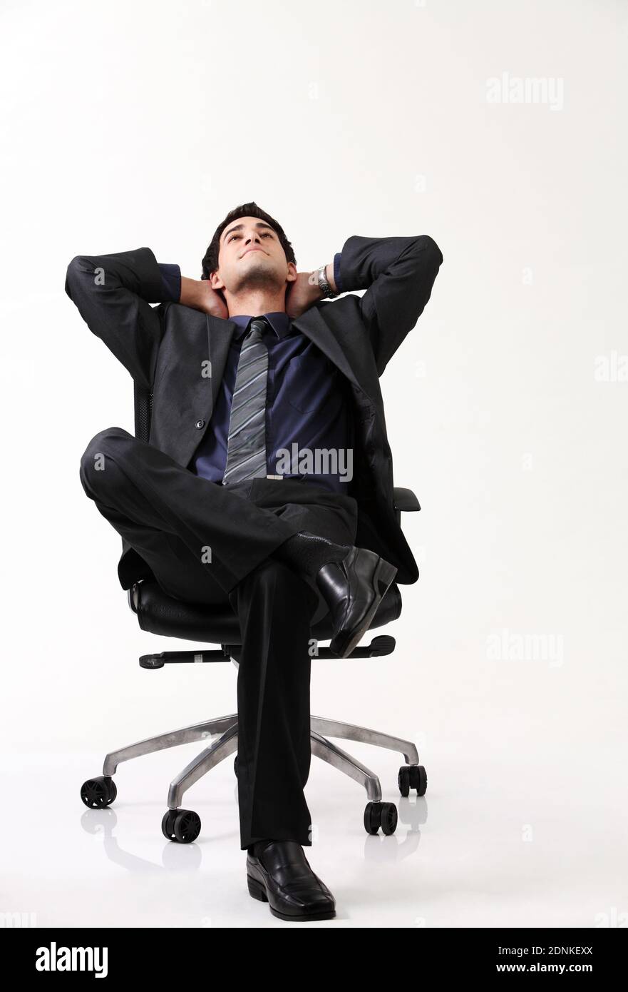 Businessman With Hands Behind Head Sitting On Chair Against White ...