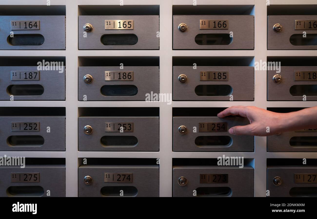 Woman hand open modern mail box of apartment filled home numbers of ...