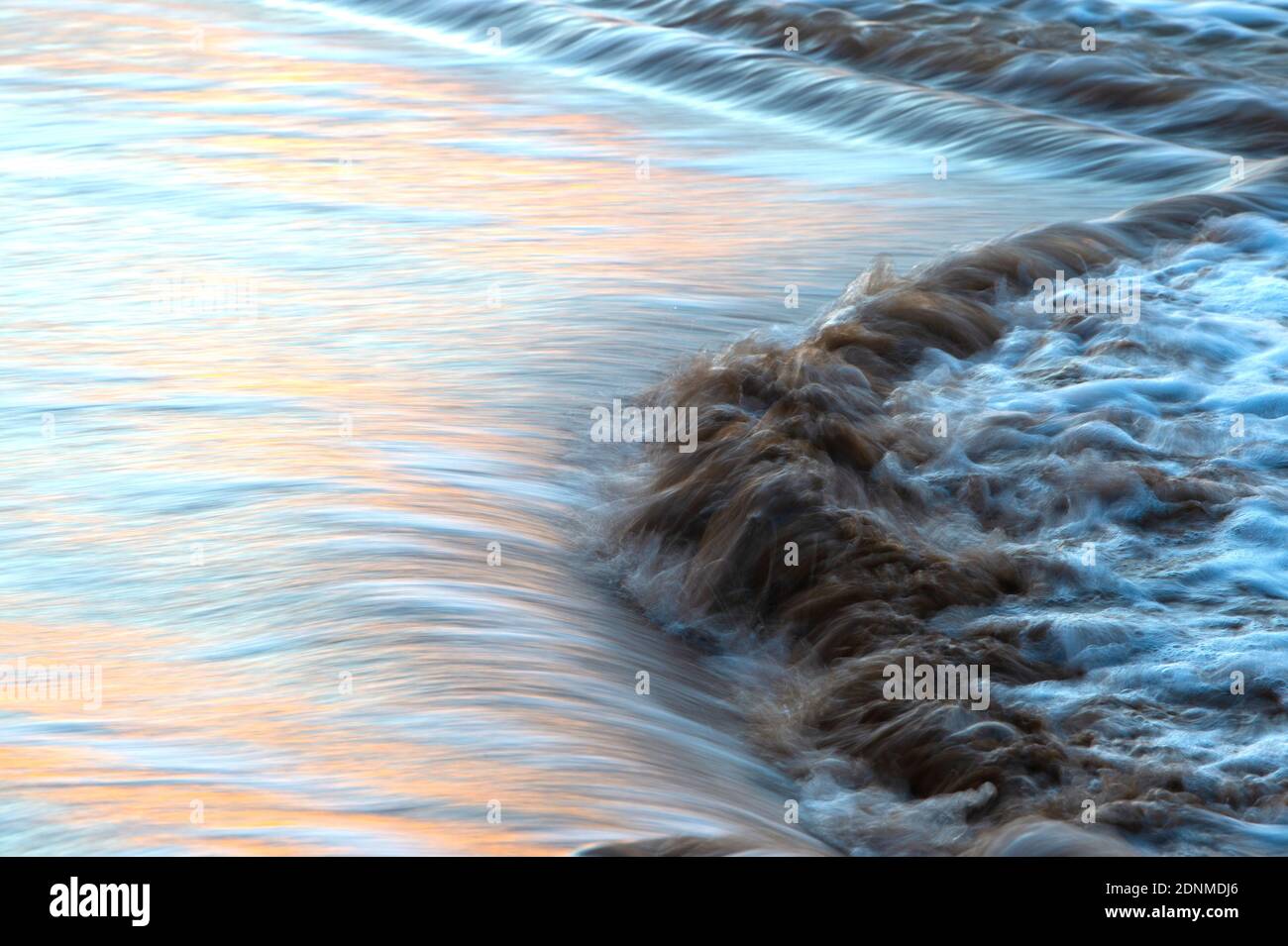 The tidal surge spills over the shallows on a beach at dusk reflecting ...