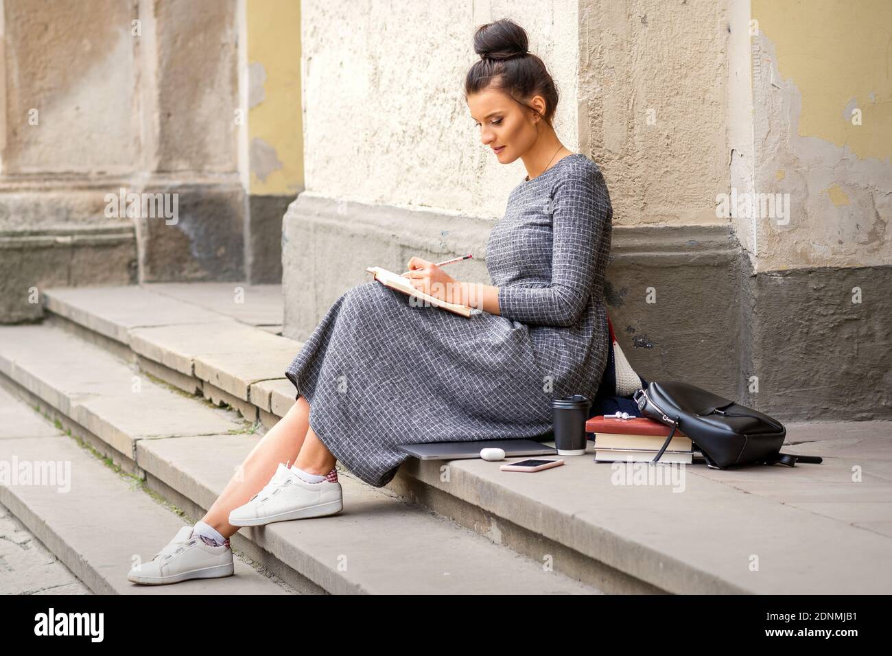 Female student in long dress reading a book on stairs of university ...