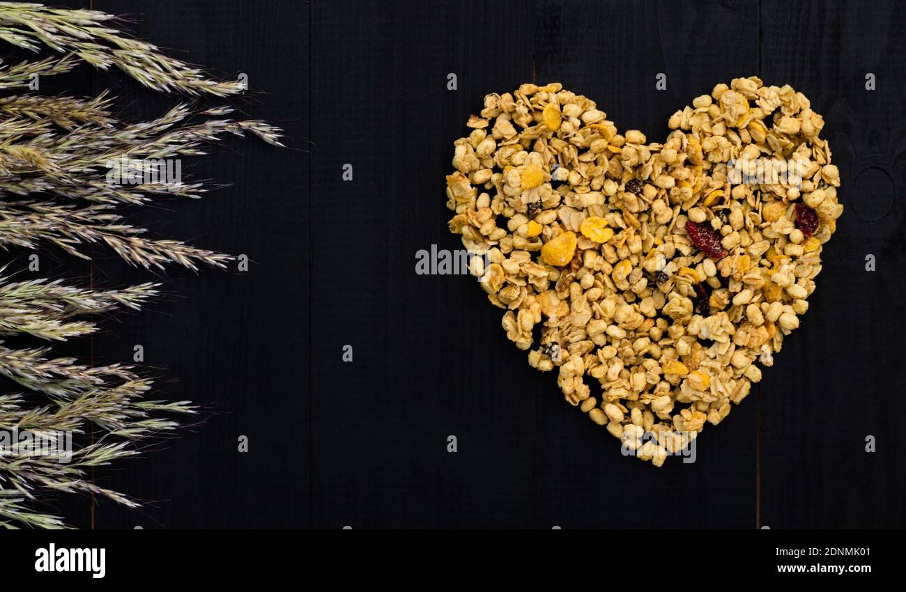 Heart laid out of granola and spikelets on a black wooden background ...
