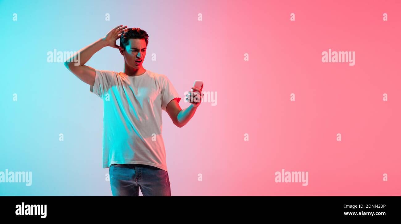 Scrolling phone. Young caucasian man's portrait on gradient blue-pink ...