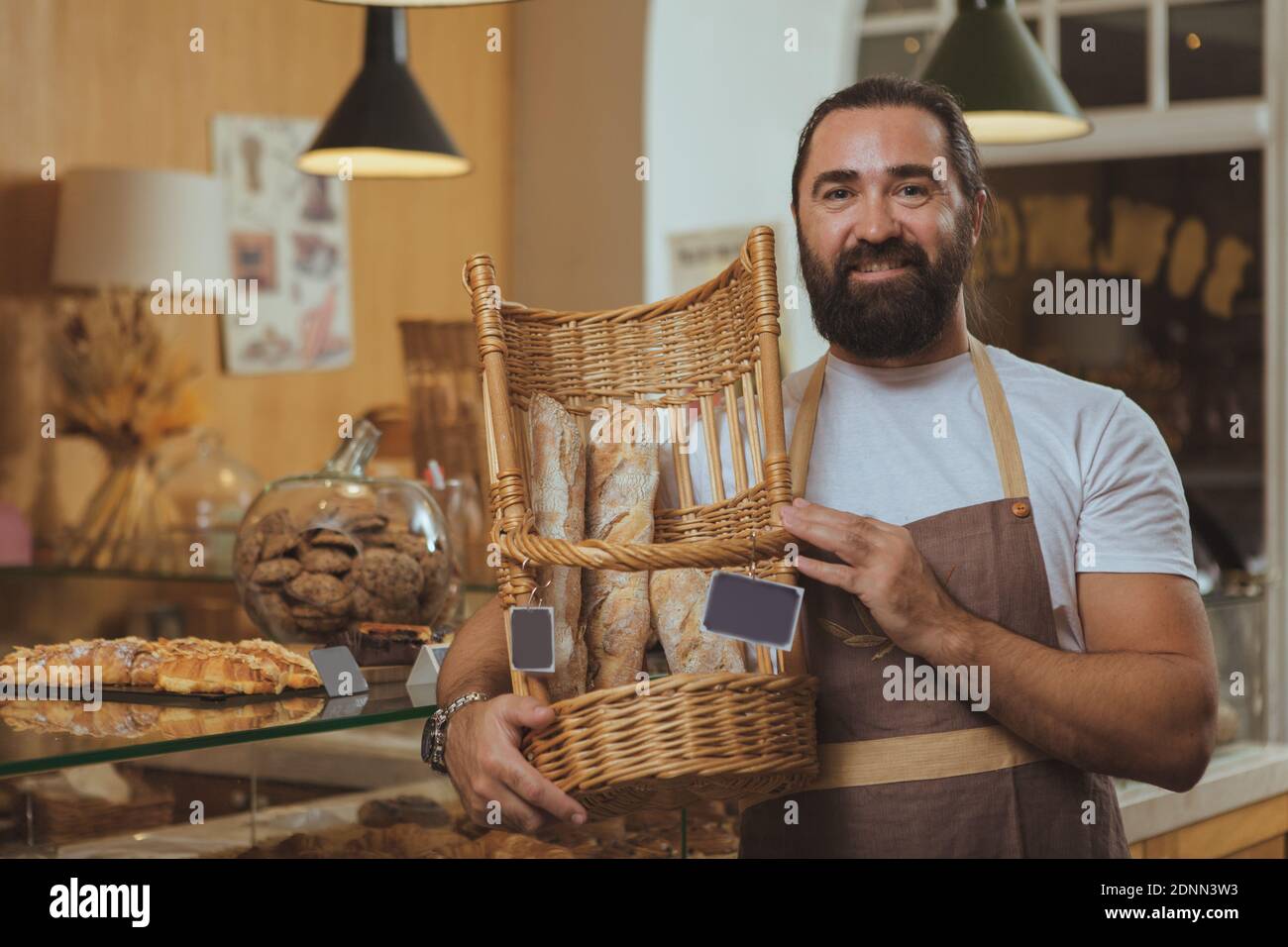 Happy handsome bearded baker wearing apron, carrying basket with fresh ...