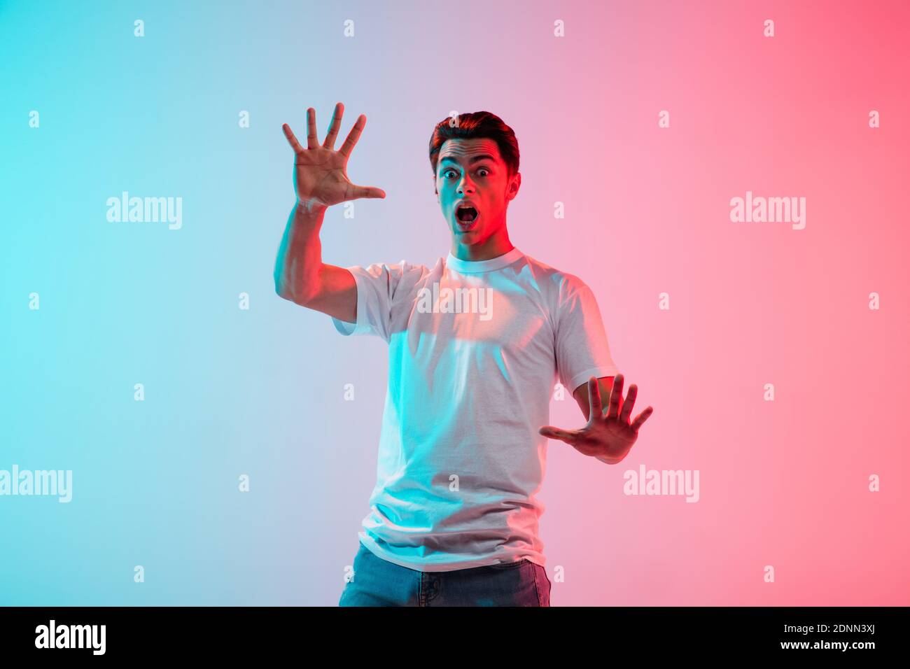 Scared, shocked. Young caucasian man's portrait on gradient blue-pink ...