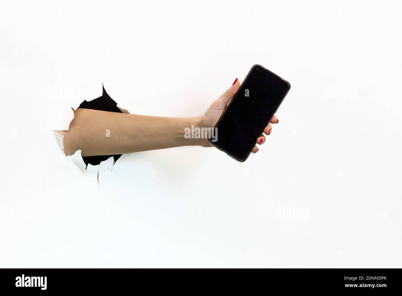 A female hand with a red manicure through torn white paper holds a ...