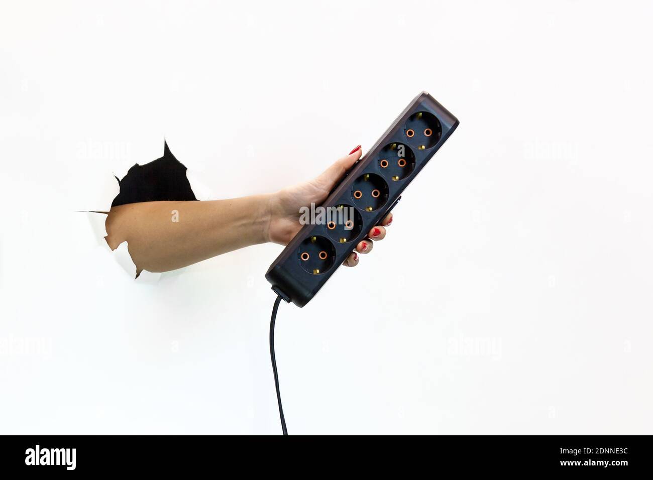 A female hand with a red manicure through torn white paper holds an ...