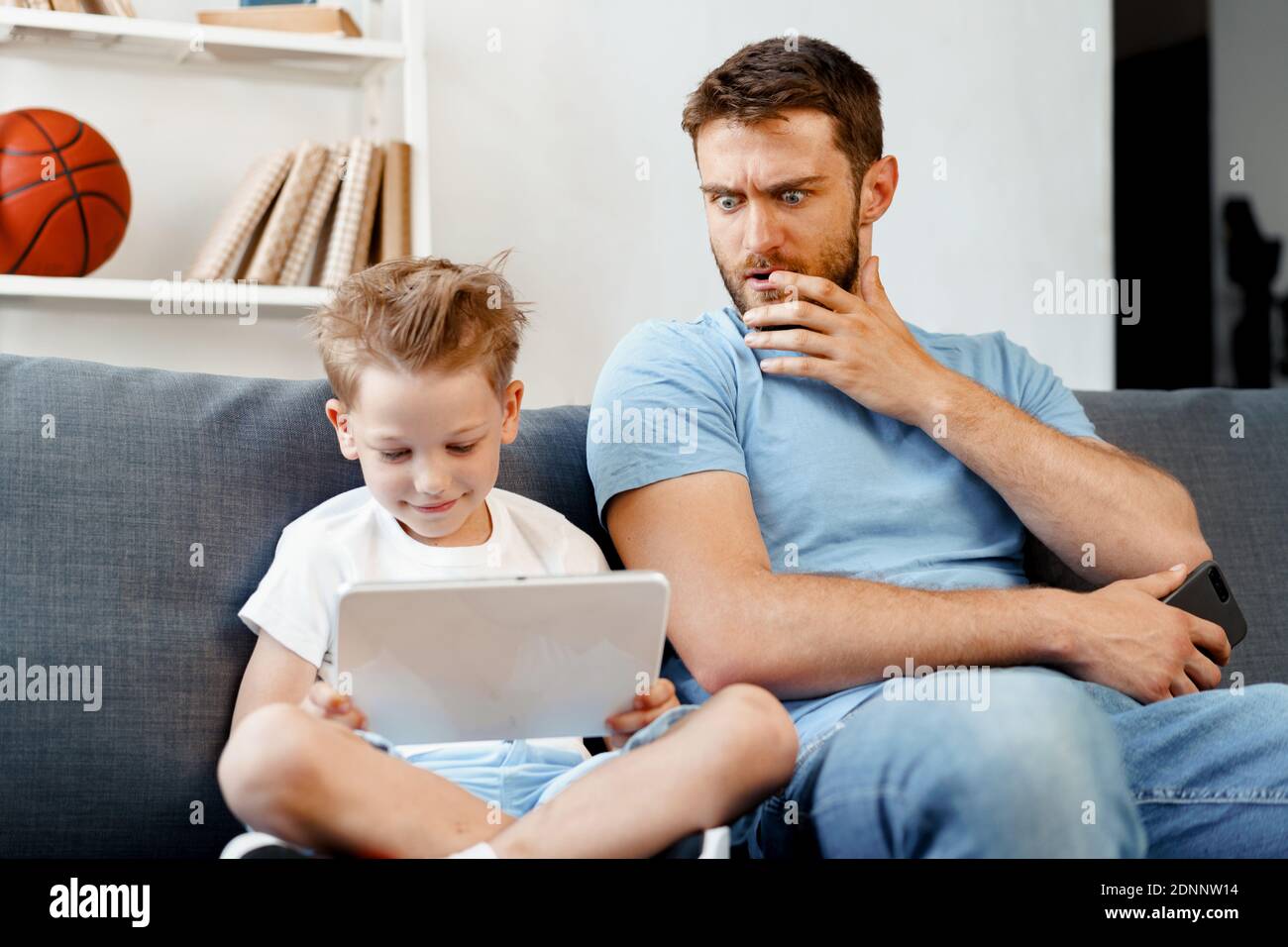 Worried father peeking at what his son is watching on digital tablet ...