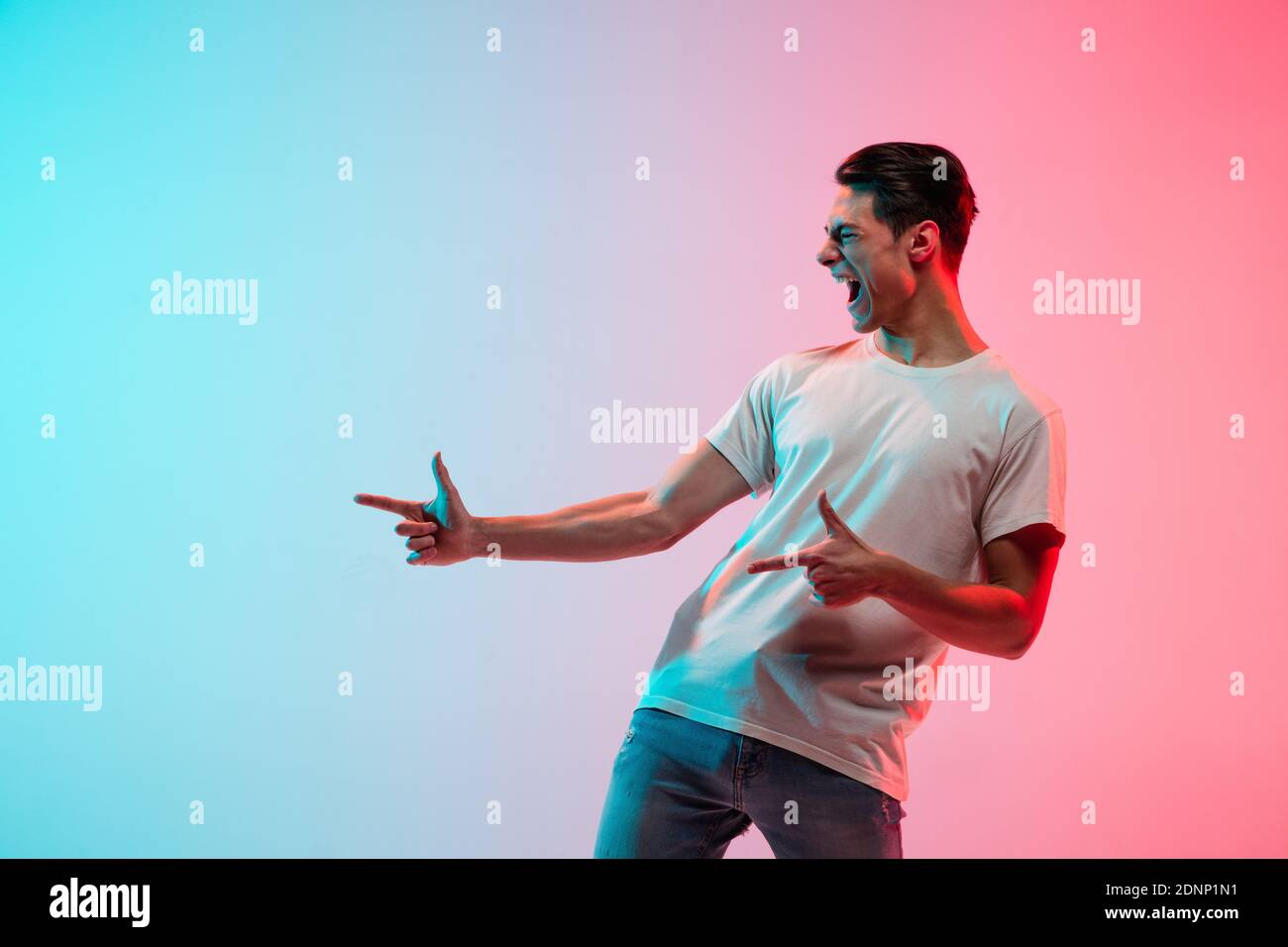 Pointing at sides, rocking. Young caucasian man's portrait on gradient ...