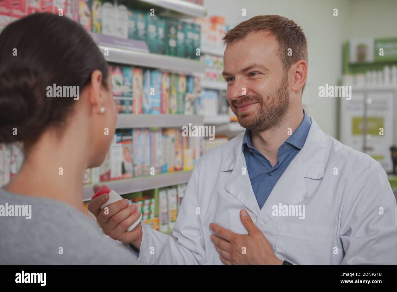Cheerful male pharmacist smiling, talking to his female customer at the ...