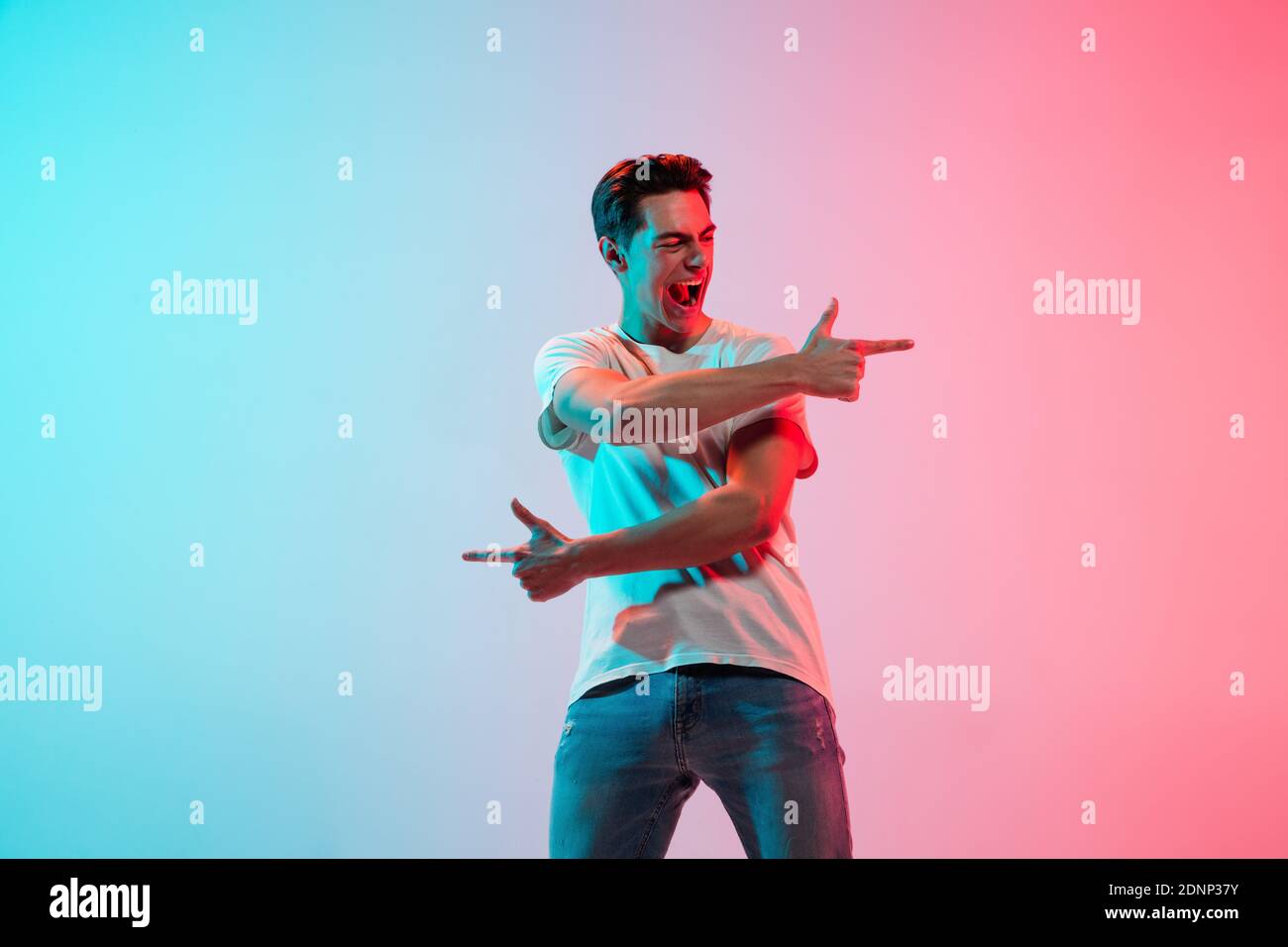 Pointing at sides, rocking. Young caucasian man's portrait on gradient ...