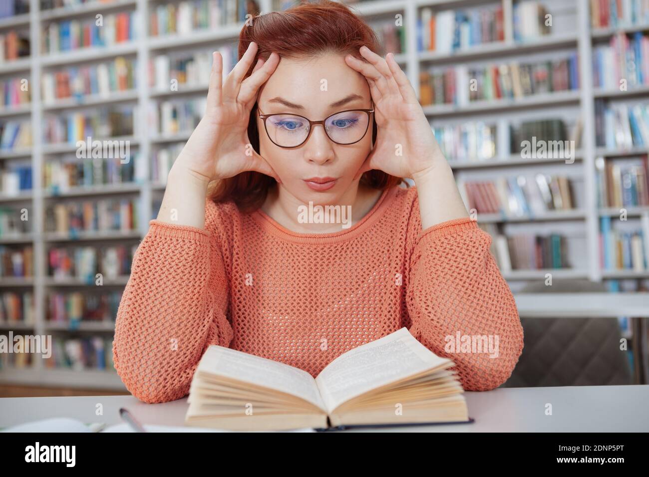 Female student stressing out over a book at the library. Tired young ...