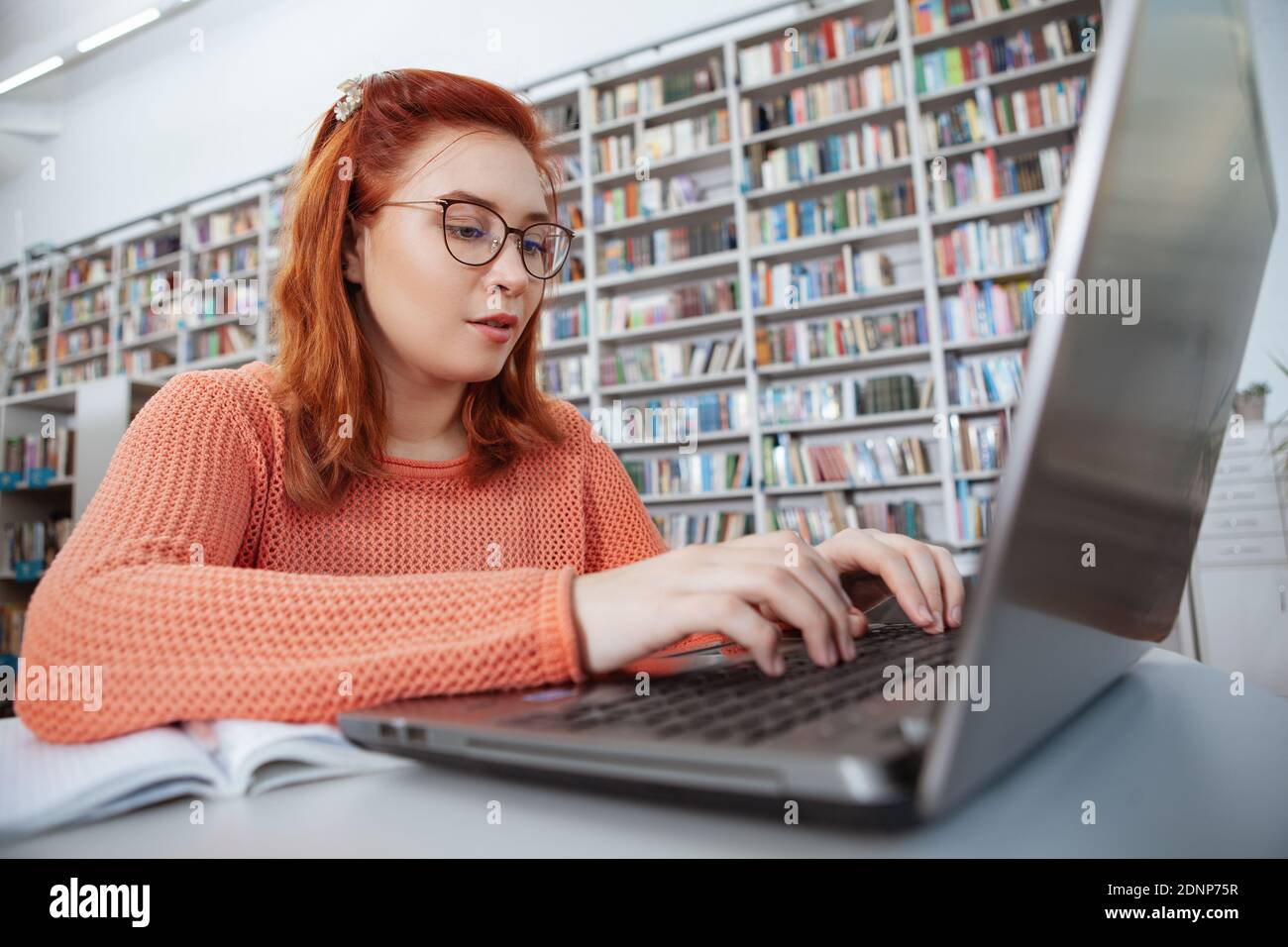Young woman working on her laptop at the library. Female student using ...