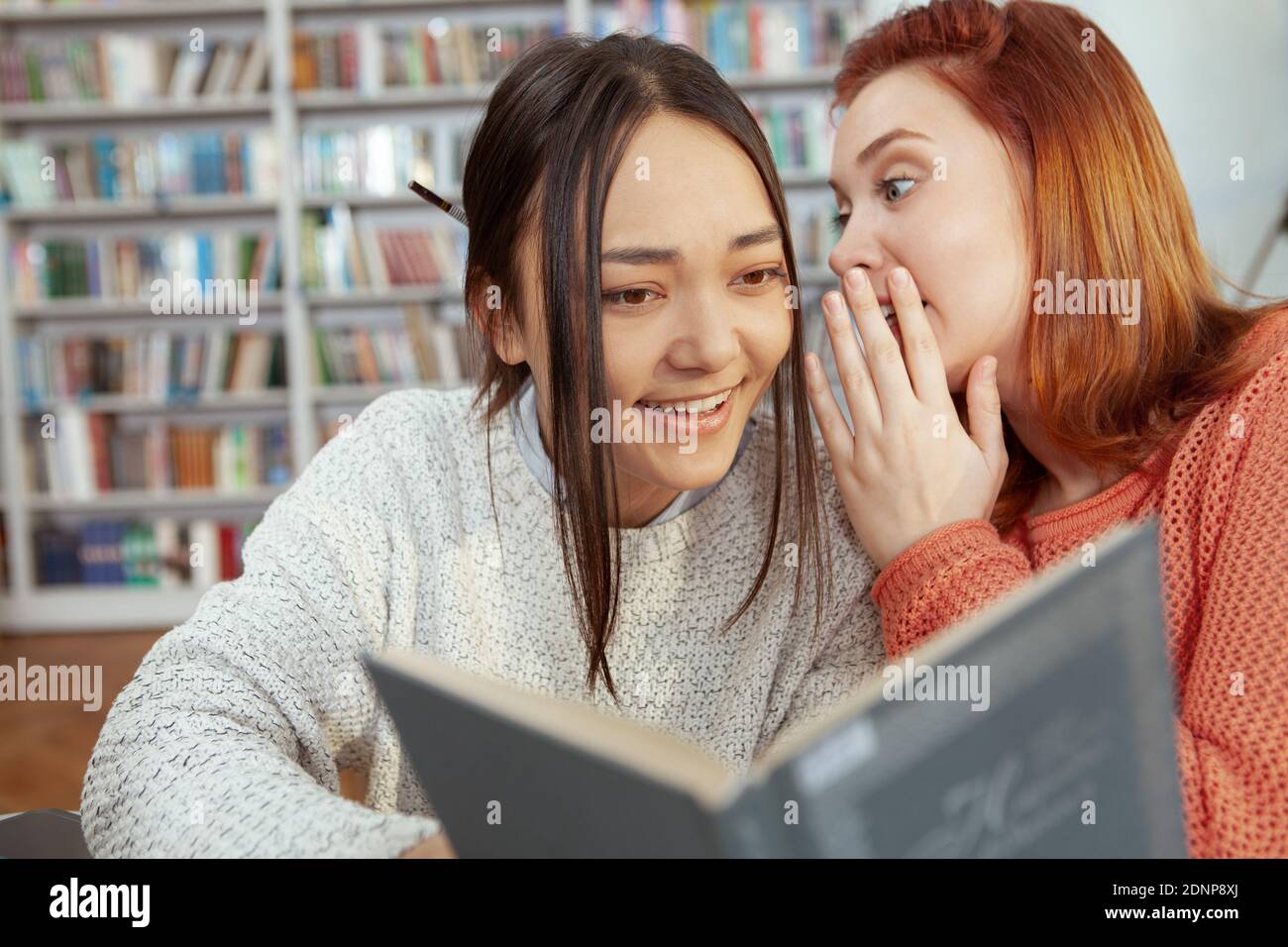 Young female students whispering quietly while studying at the library ...