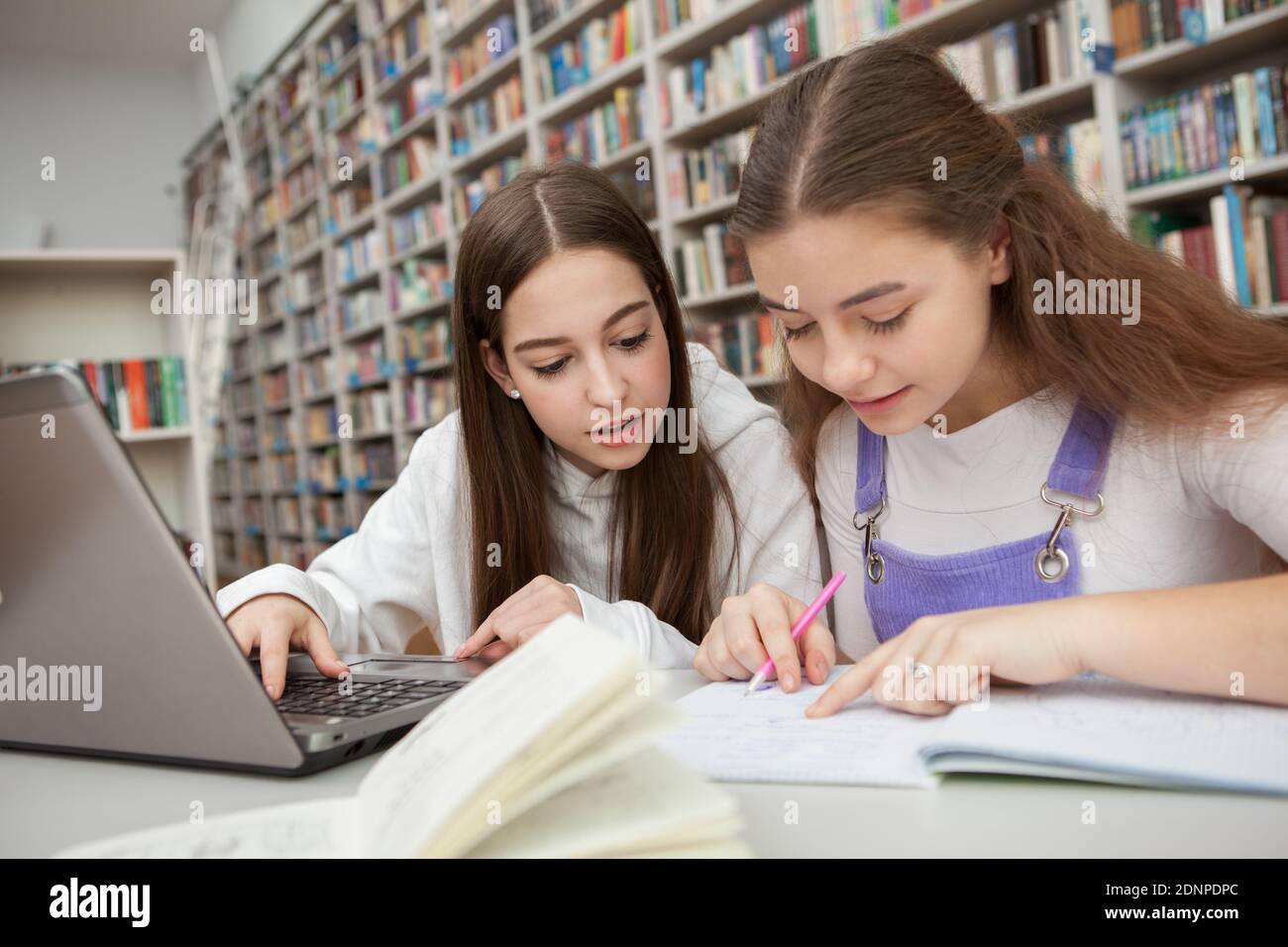 Two teen schoolgirls working on a project together at the library ...