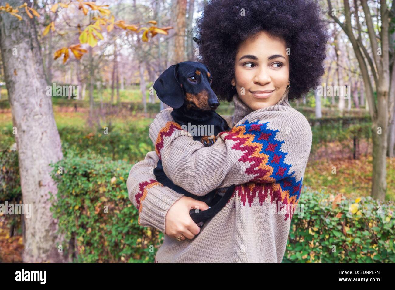 African American girl sitting and hugging her dog in the park in autumn ...