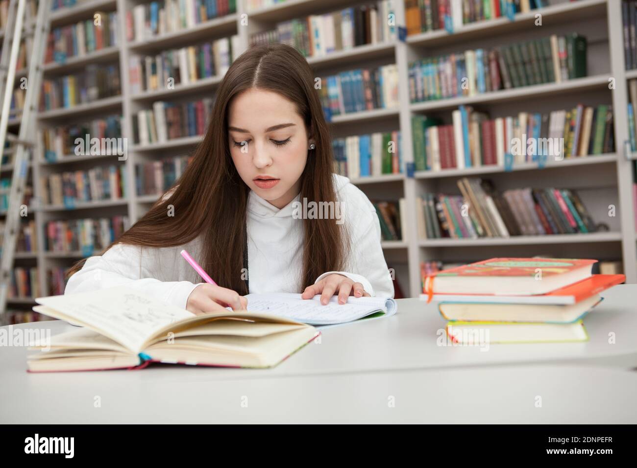 Young teenage girl looking concentrated, writing in her textbook at the ...