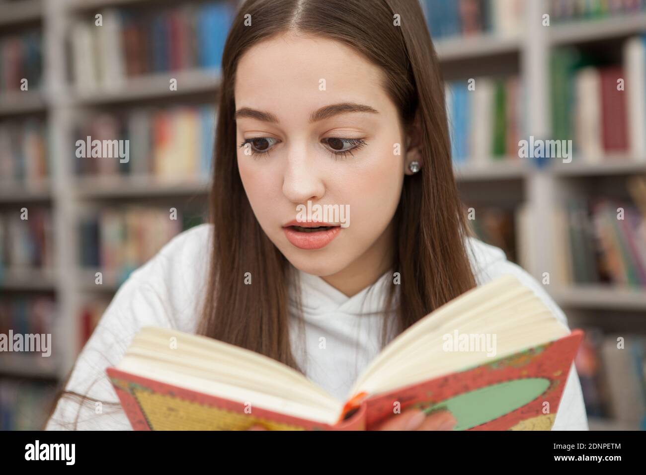 Close up of a teenage girl looking overwhelmed, reading a book at the ...